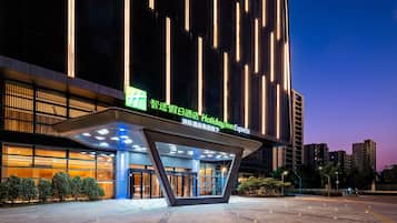 Fachada moderna de hotel com sinalização iluminada, área de entrada coberta e boa iluminação.