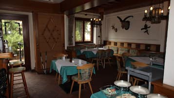 Restaurante com mesas e cadeiras de madeira, toalhas de mesa cor verde-água e decoração rústica, incluindo chifres na parede.