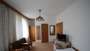 Quarto de hotel com duas camas individuais, um sofá, uma televisão e uma mesa de trabalho com telefone.