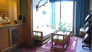 Uma área de recepção com balcão de madeira, mesa, cadeiras, uma janela grande com cortinas e iluminação embutida no teto.