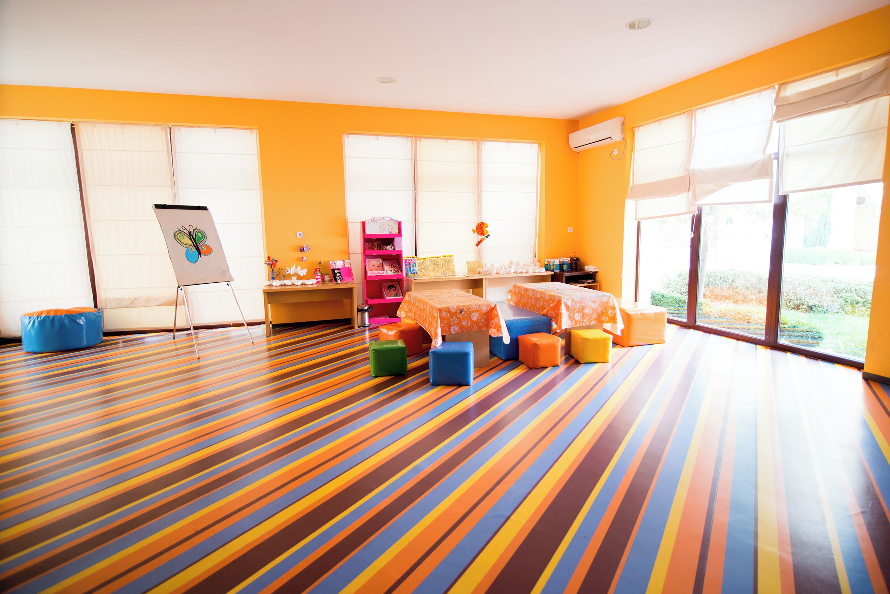 Um quarto vibrante com piso listrado, uma escrivaninha com computador, uma cama e uma janela com persianas.