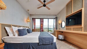 Quarto de hotel moderno com uma cama grande, um ventilador de teto, televisão na parede e varanda com vista.