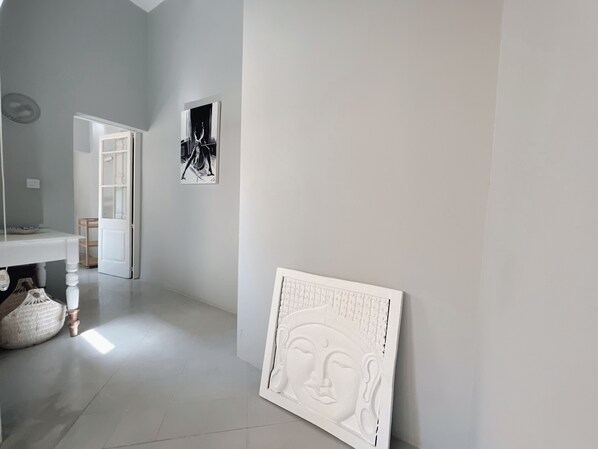Um corredor com uma porta branca, uma parede branca com um relevo e uma fotografia a preto e branco emoldurada na parede.