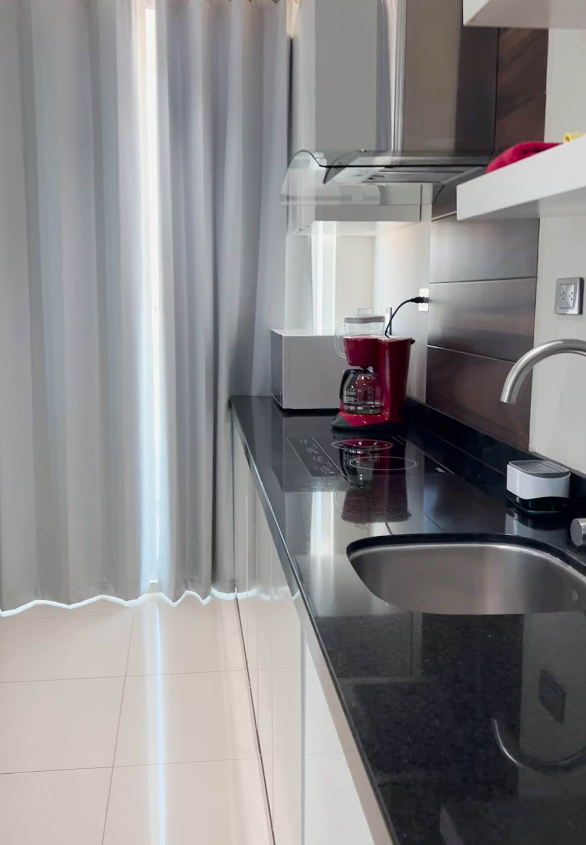 Uma cozinha moderna com uma pia de aço inoxidável, uma cafeteira vermelha e uma bancada elegante.