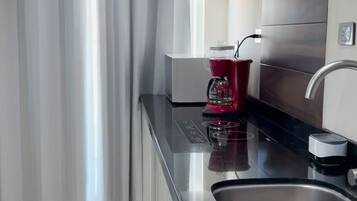 Uma cozinha moderna com uma pia de aço inoxidável, uma cafeteira vermelha e uma bancada elegante.