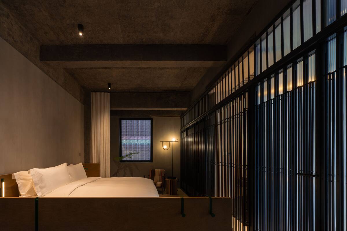 Quarto de hotel moderno com cama, janela grande e vista para o exterior.
