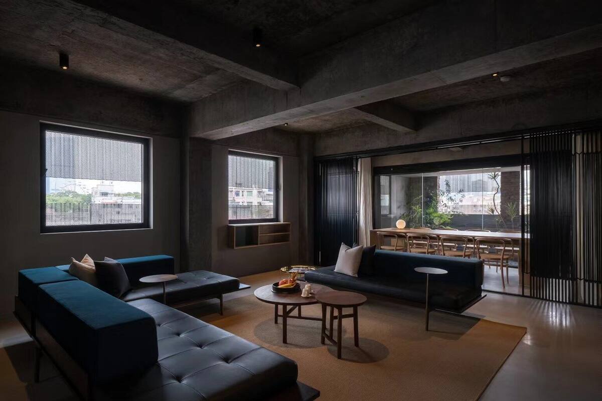 Uma sala de estar moderna com um sofá seccional, uma mesa de centro redonda e uma área de jantar com mesa e cadeiras. Janelas amplas oferecem luz natural e vista da cidade.