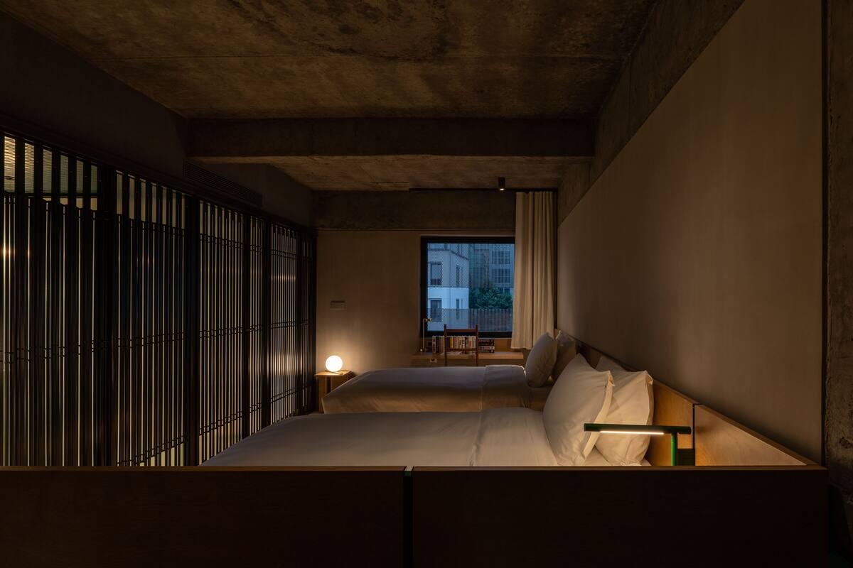 Quarto com cama, mesa de cabeceira e janela com vista para edifícios.