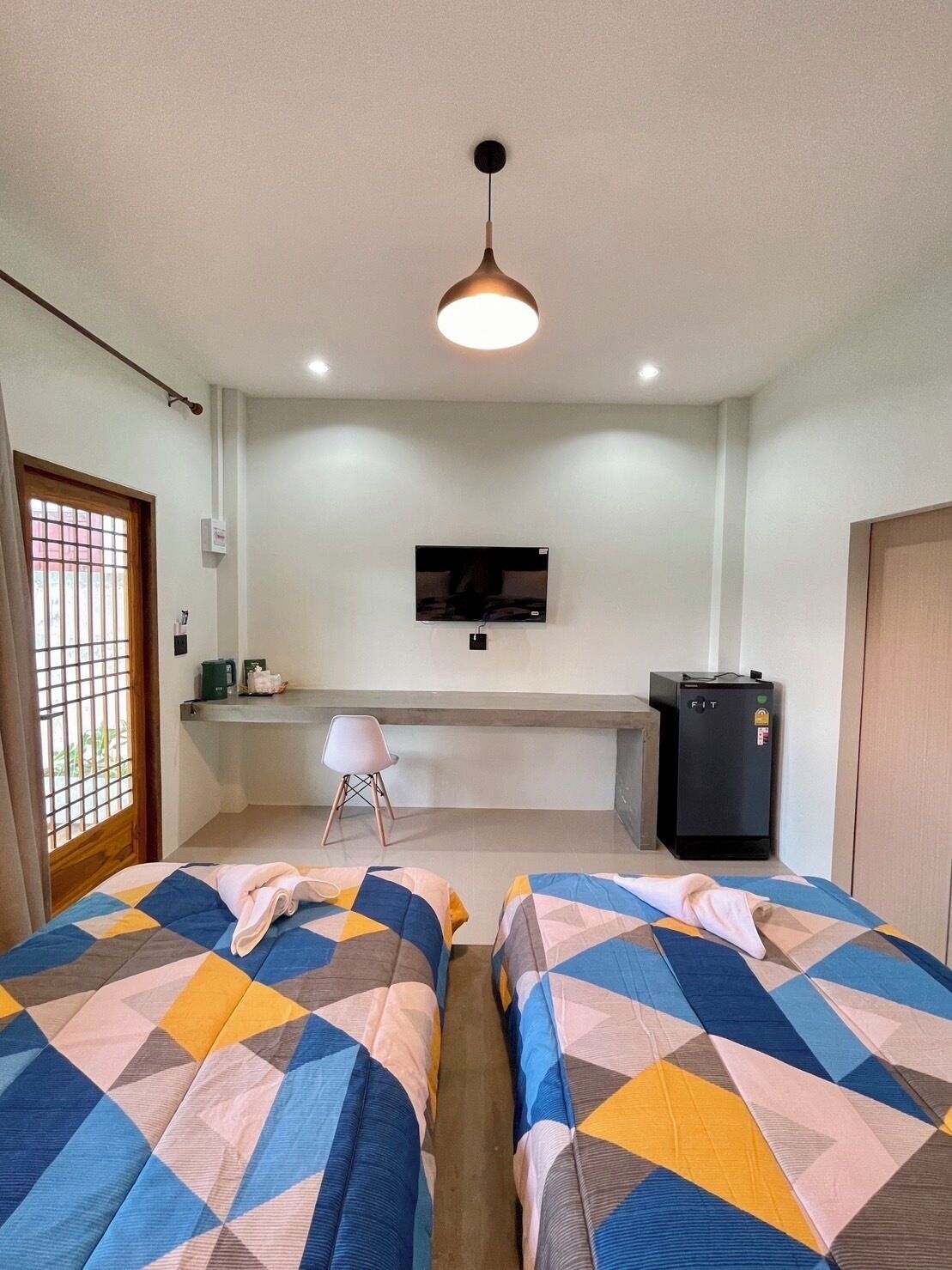 Quarto de hotel com duas camas, televisão na parede, uma secretária pequena e um frigorífico.