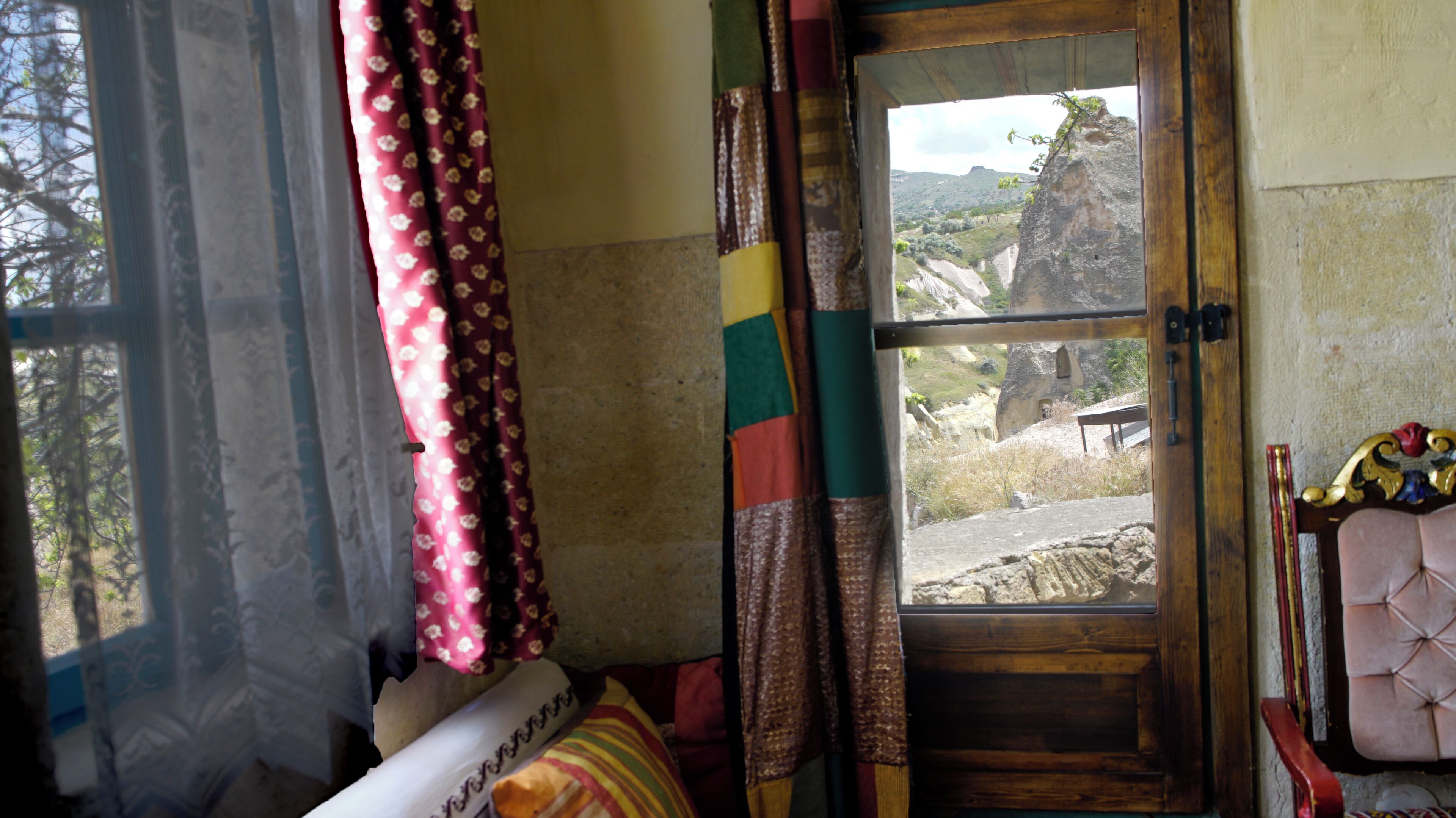 Um quarto com uma cama, uma janela com cortinas e vista para uma paisagem montanhosa.