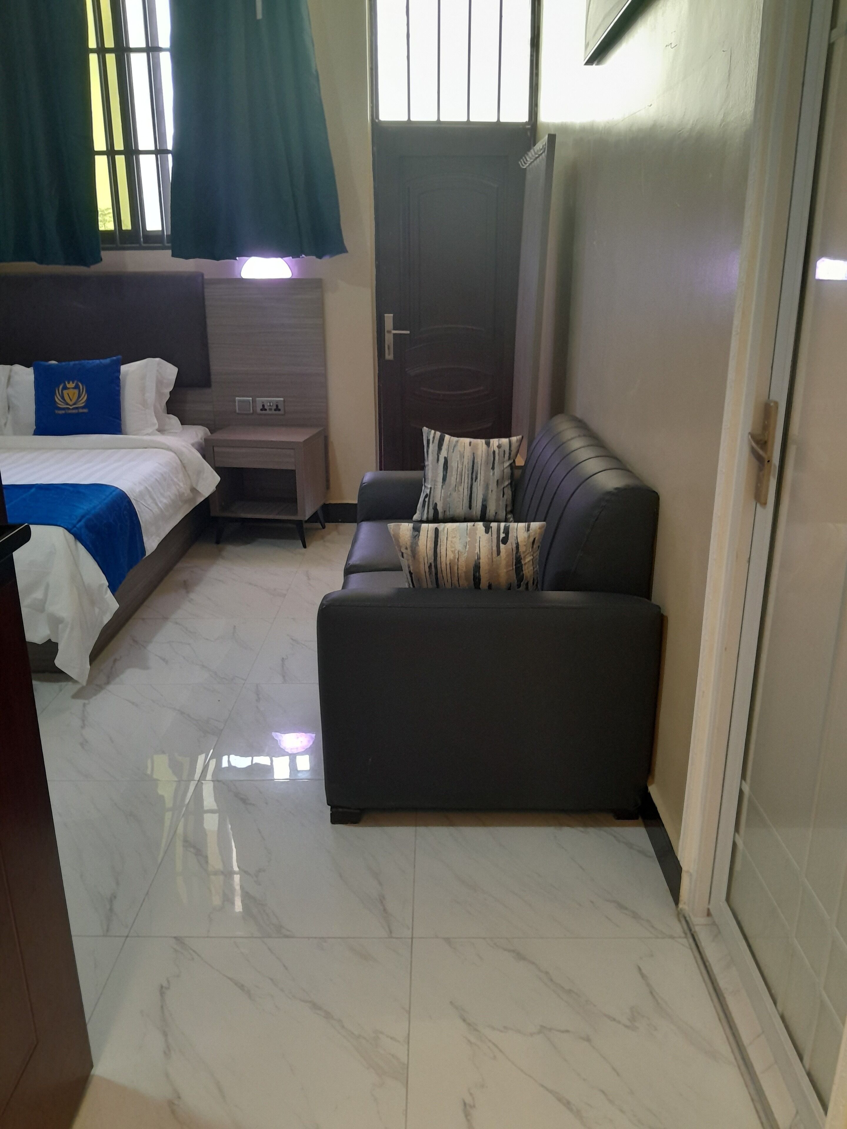 Quarto de hotel pequeno com cama, sofá, mesa de cabeceira e porta.