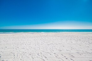 Uma extensa praia de areia dourada, com águas azul-claras e céu limpo.
