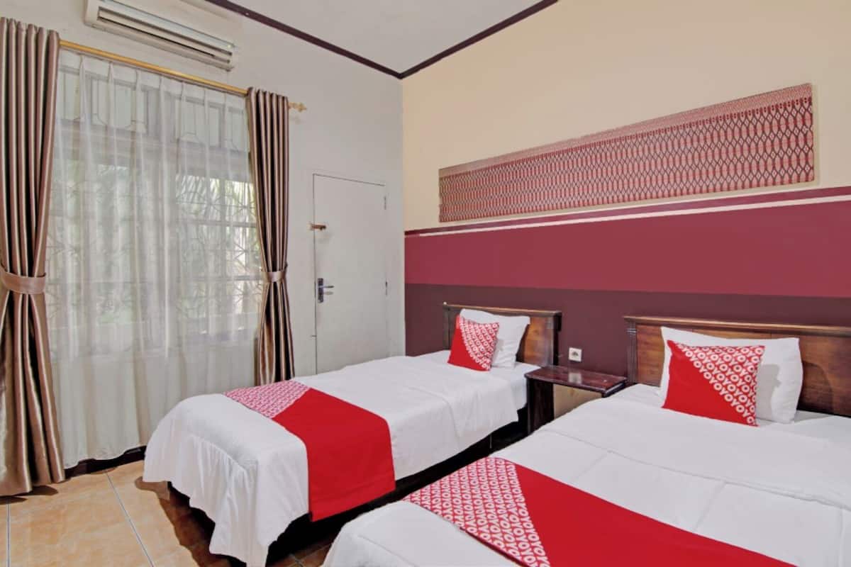 Quarto de hotel com duas camas, janela com cortinas, ar condicionado fixado na parede e painel decorativo sobre as camas.