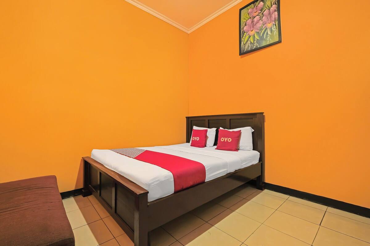 Quarto com cama, um banco e um quadro na parede.