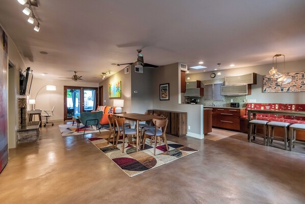 Ampla sala de estar com mesa de jantar, cadeiras, sofá e cozinha equipada com eletrodomésticos modernos.