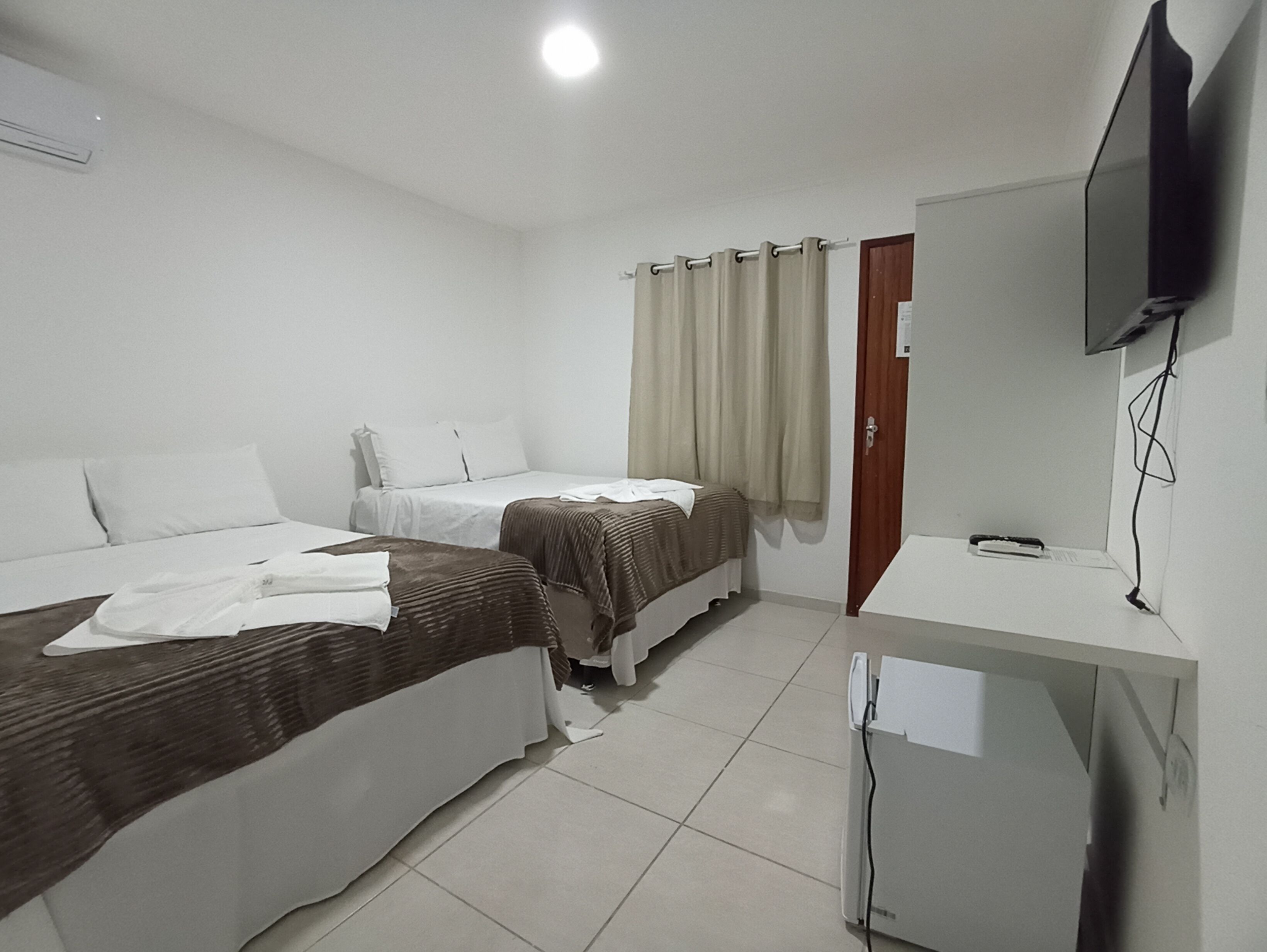 Quarto de hotel com duas camas, uma televisão e uma pequena mesa.