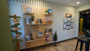 Uma área de recepção com um sinalizador de madeira, prateleiras com livros e objetos decorativos, e um sinal indicando 'BIKE'.