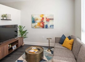 Uma sala de estar moderna com televisão de tela plana, um sofá, uma mesa de centro e um quadro na parede.