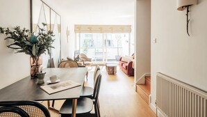 Uma área de refeições com mesa, cadeiras e um vaso de plantas. Há uma janela com vista para o exterior.