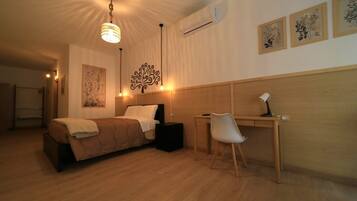 Quarto com cama, mesa de cabeceira, cadeira, escrivaninha, luminária, quadro na parede e ar condicionado.
