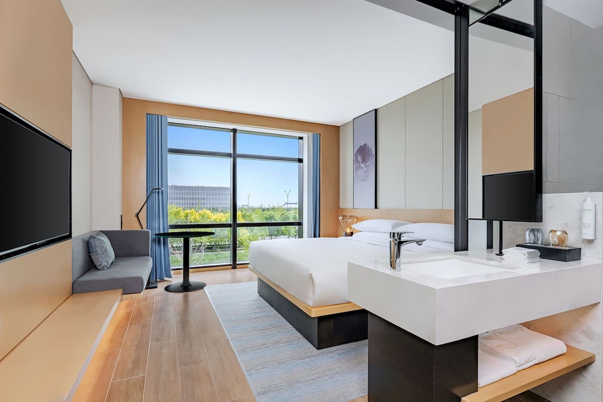 Quarto de hotel moderno com uma cama grande, pia dupla, TV de tela plana e sofá.