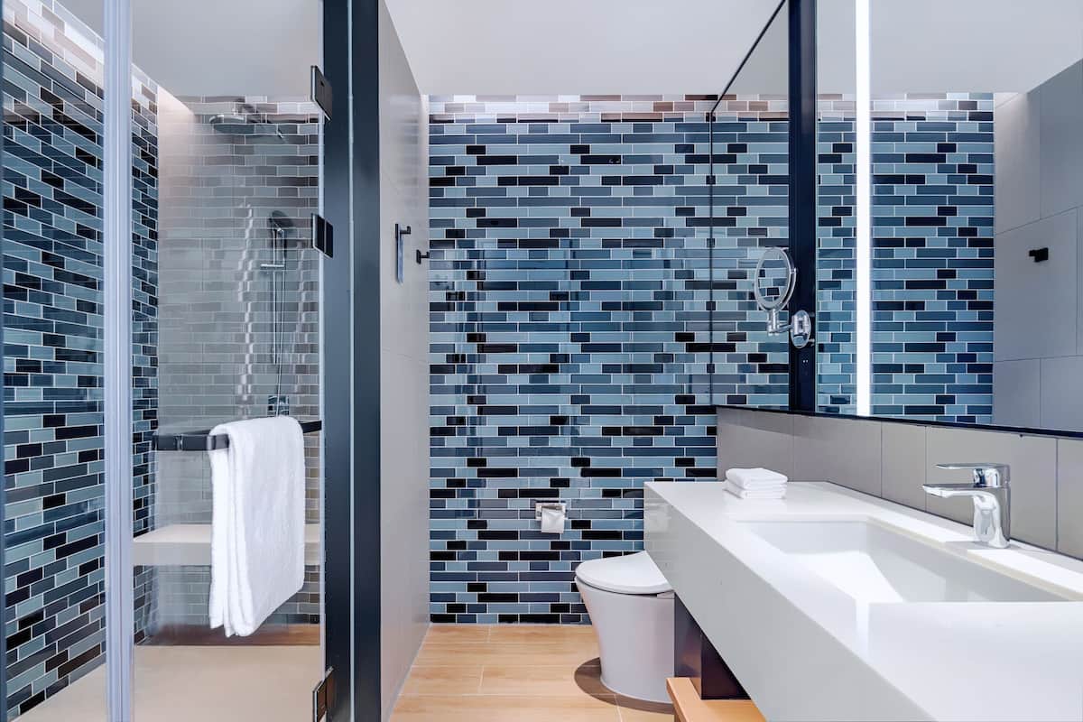 Casa de banho moderna com cabine de duche em vidro, lavatório branco e painel de azulejos.