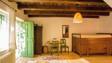 Quarto com teto de madeira, porta verde, cômoda de madeira, mesa com cadeiras e uma cama.