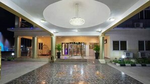 Entrada de hotel com piso de mármore, luminária circular no teto e porta giratória.