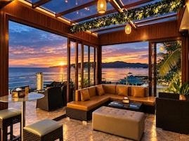 Uma área de estar moderna com um sofá grande, uma mesa redonda e cadeiras de vime, com vista para um pôr do sol deslumbrante.