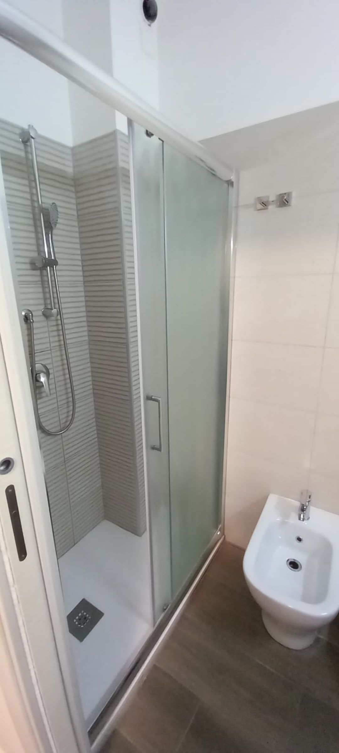 Um chuveiro envidraçado com barra de mão e torneira fixa na parede.