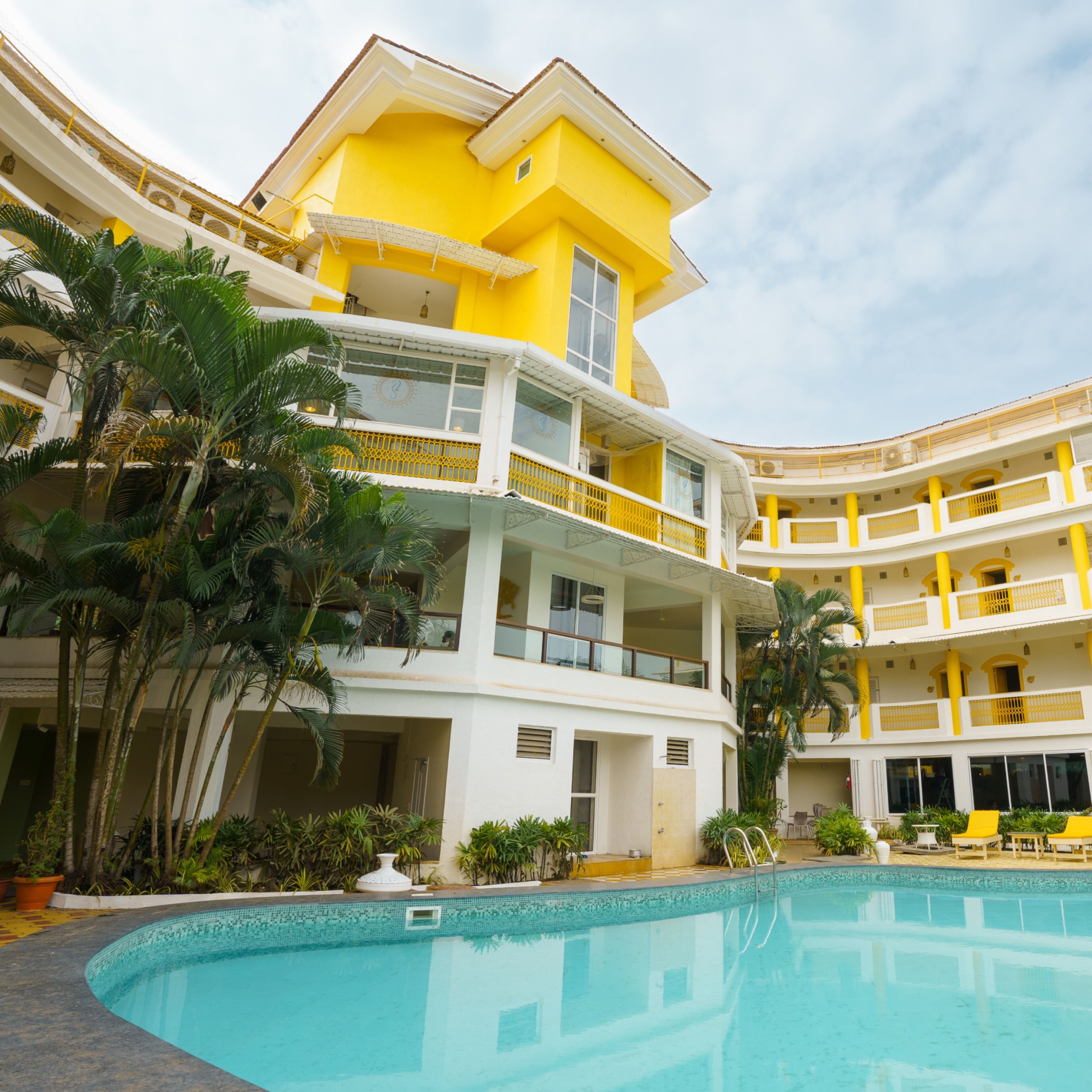Um hotel de vários andares com piscina, varandas e plantas tropicais.