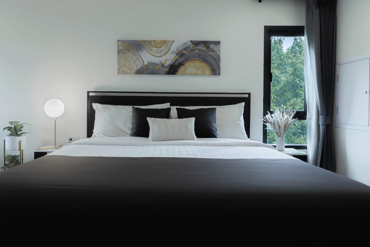 Quarto moderno com uma cama grande, mesa de cabeceira com luminária e janela com vista para o verde.