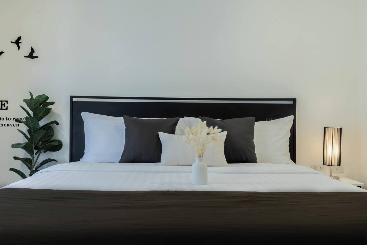 Uma cama bem arrumada com roupa de cama branca e um vaso de flores secas no centro.