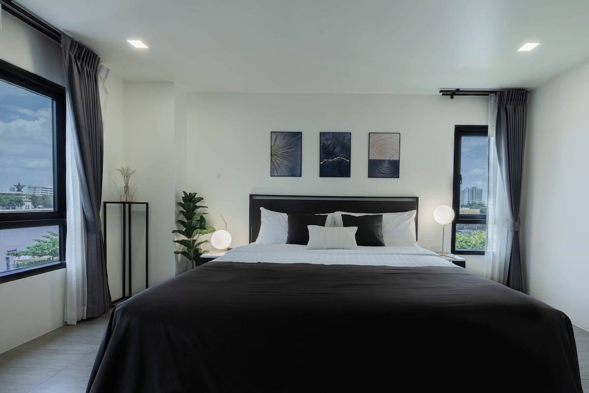 Quarto de hotel moderno com uma cama grande, uma mesa de cabeceira com abajur e três obras de arte na parede acima da cama.
