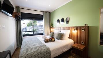Quarto de hotel com cama, mesa de cabeceira, janela com cortinas, TV na parede e vista para o exterior.