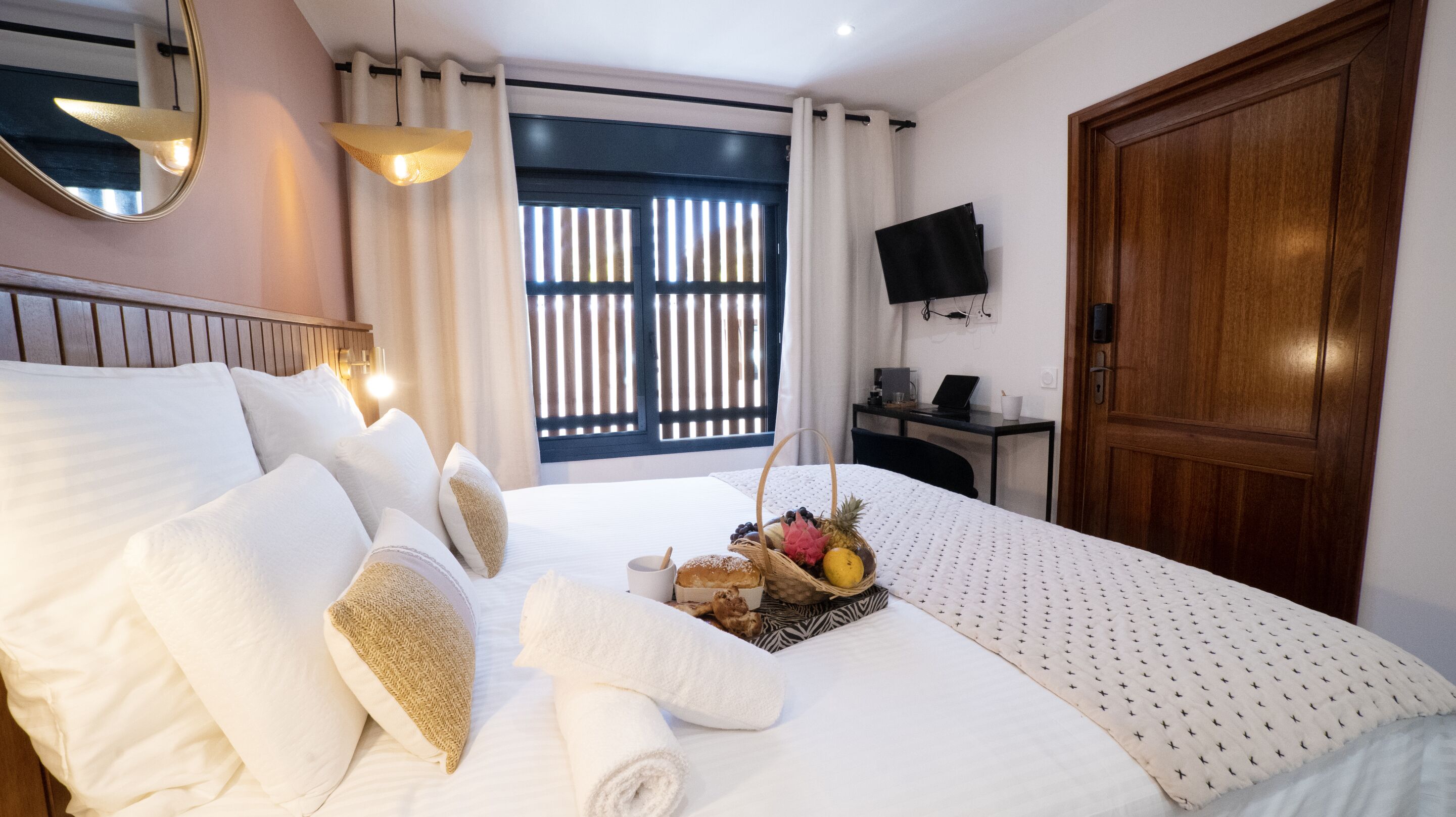 Quarto de hotel com cama, escrivaninha, televisão e janela com persianas.