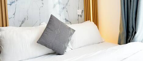 Quarto de hotel com parede estampada em mármore, cama com roupa de cama branca, travesseiro com padrão preto e branco, e cortina.