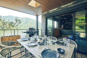Uma área de refeições com uma mesa posta para seis pessoas, rodeada por cadeiras de vime, com vista para uma paisagem montanhosa.