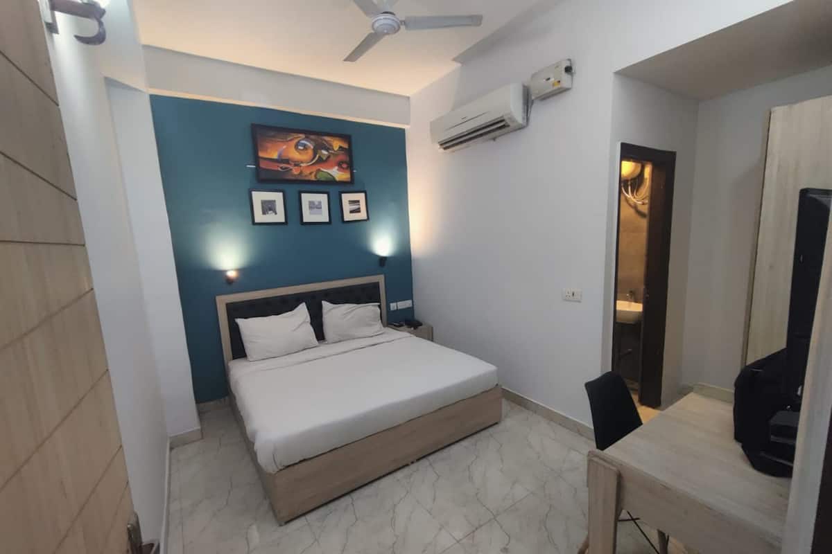 Quarto com cama, ventilador de teto, ar condicionado, escrivaninha e TV fixada na parede.