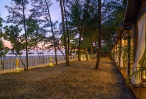 Um caminho à beira-mar ladeado por árvores e um deck de madeira com cortinas brancas.