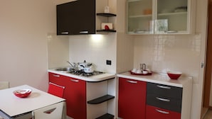Cozinha compacta com armários vermelhos e brancos, fogão a gás, pia e área de refeições com mesa e cadeiras.