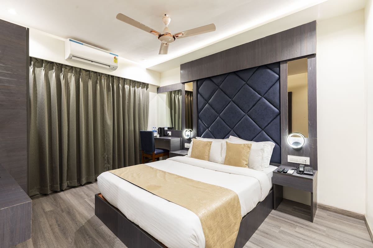 Quarto de hotel moderno com uma cama grande, uma mesa, uma cadeira, toucador com espelho e ar condicionado.