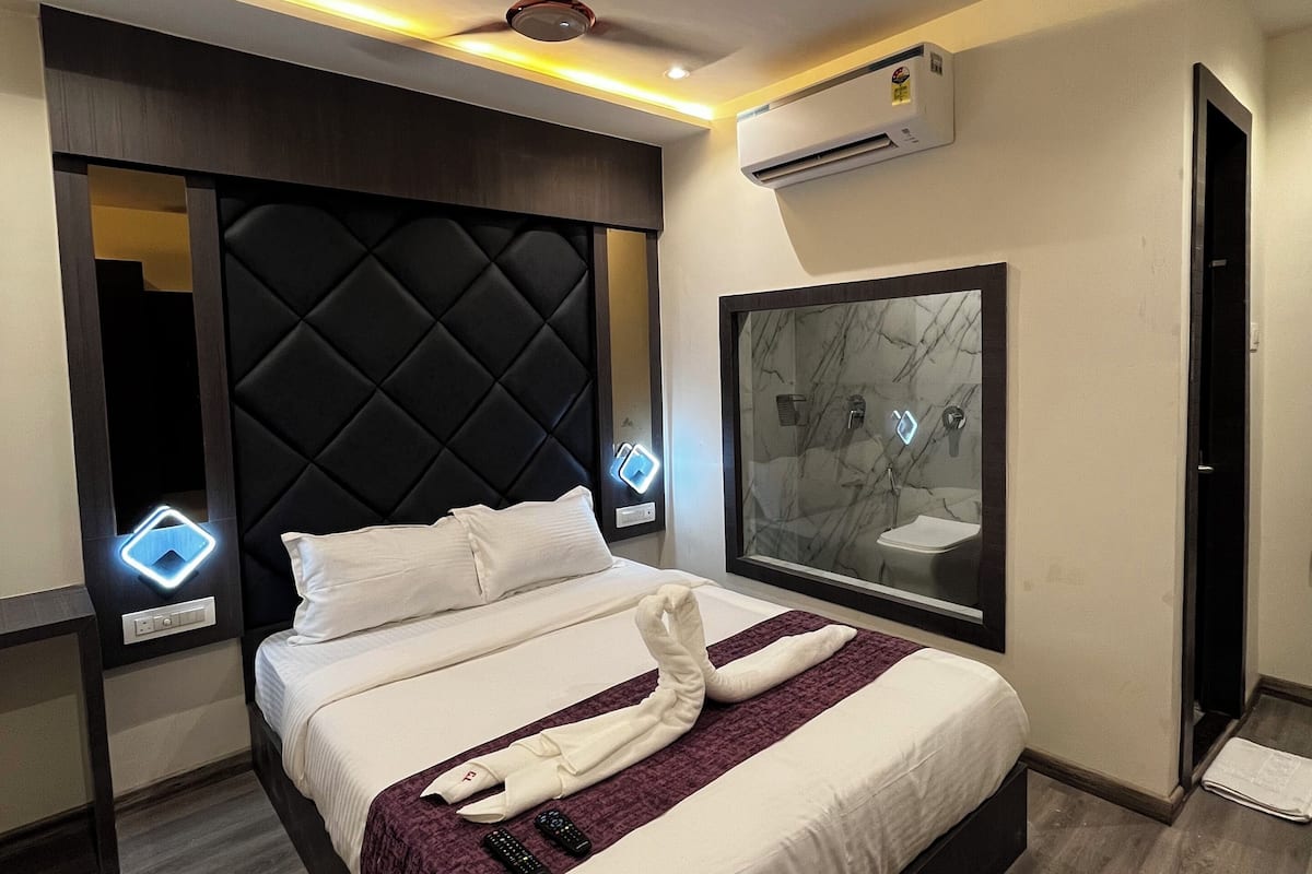 Quarto de hotel moderno com uma cama grande, cabeceira escura, ar condicionado fixado na parede e um espelho amplo.