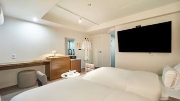 Quarto de hotel moderno com uma cama grande, uma escrivaninha com abajur, toucador com espelho e uma televisão na parede.