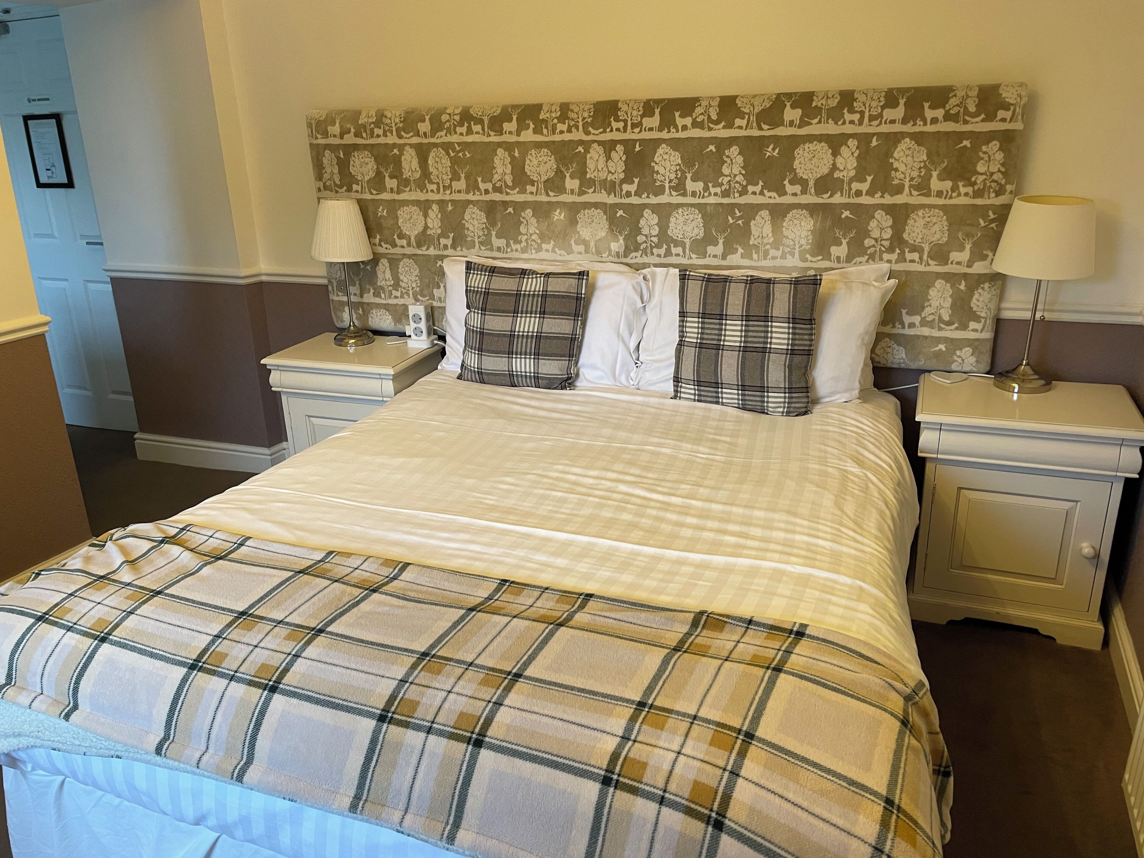 Quarto de hotel com uma cama grande, duas mesas de cabeceira com luminárias, cabeceira com design inspirado na natureza e um quadro na parede.