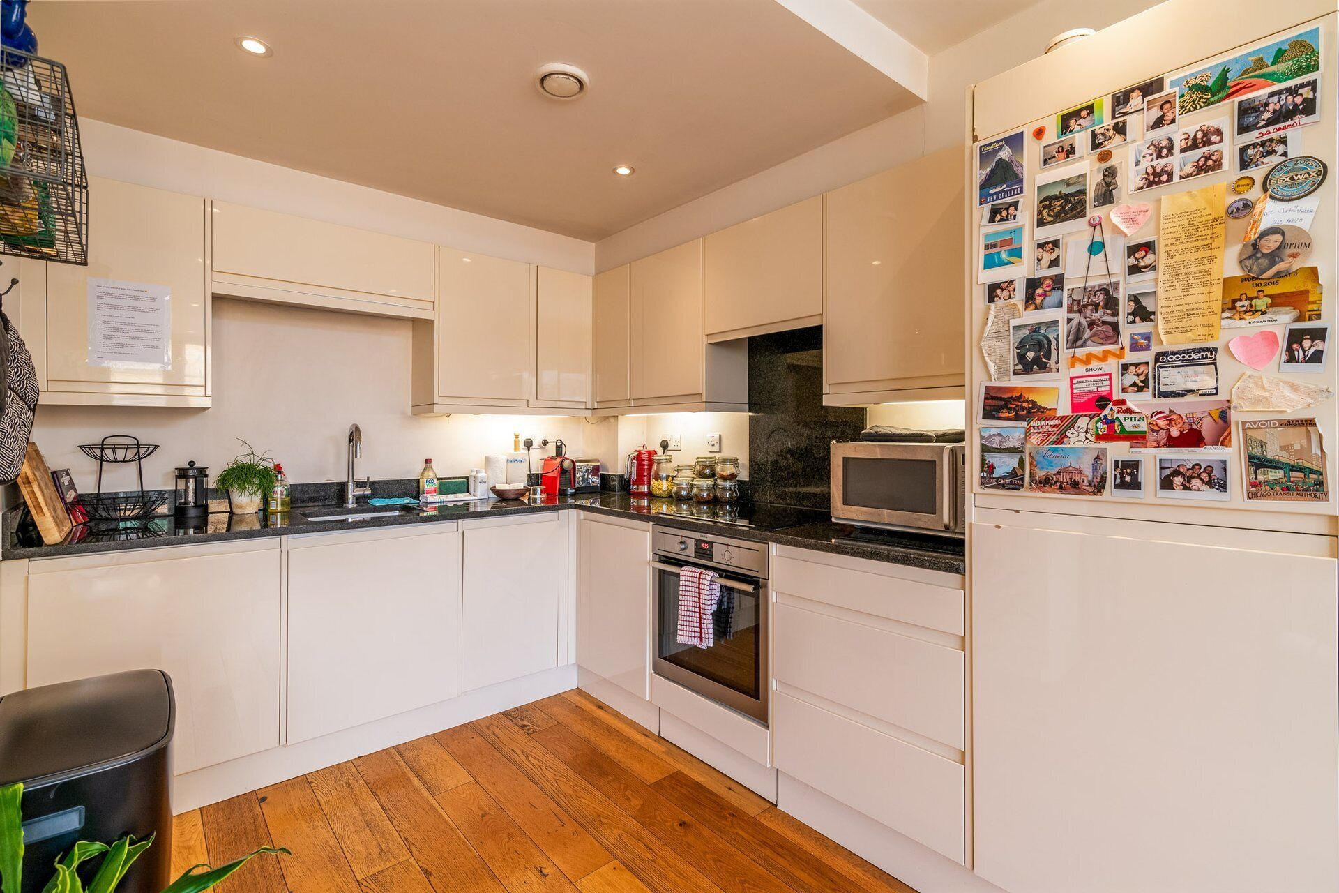Uma cozinha moderna com armários brancos, bancada preta e geladeira decorada com fotos e imãs.