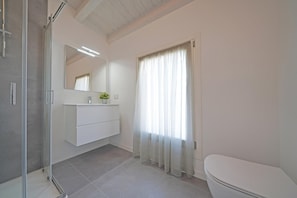 Uma casa de banho moderna com cabine de duche em vidro, toucador branco com espelho e sanita.