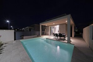 Piscina ao ar livre moderna com área de estar coberta, incluindo mesa e cadeiras.