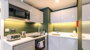 Uma cozinha compacta com micro-ondas, torradeira, chaleira e pia.