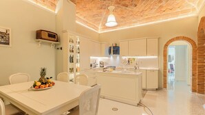 Uma cozinha moderna com armários brancos, uma ilha central e uma área de jantar com mesa e cadeiras brancas.